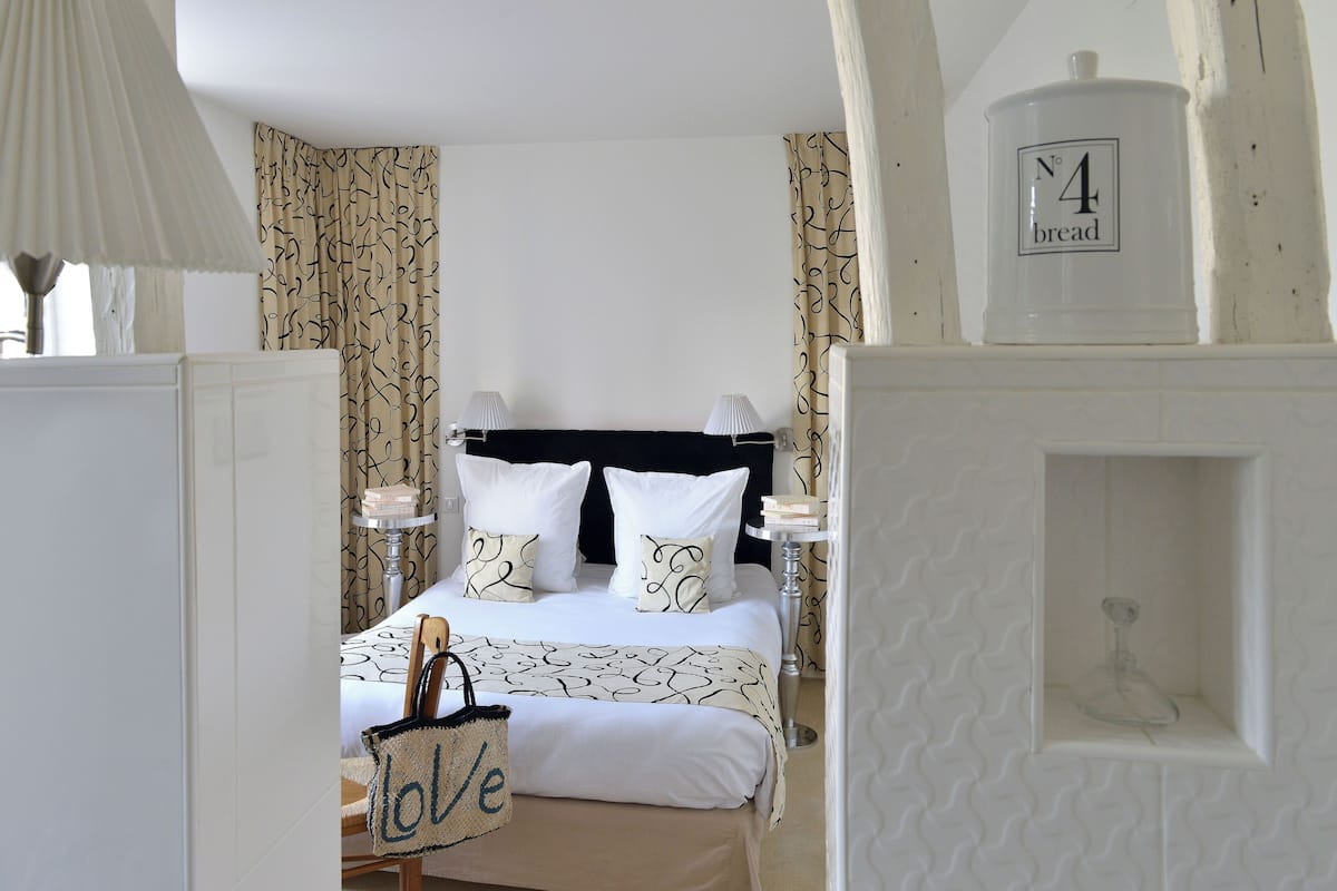 Quarto bem arrumado com cama, abajures, mesa de cabeceira, objeto decorativo com a inscrição "No 4 bread" e cortina estampada.