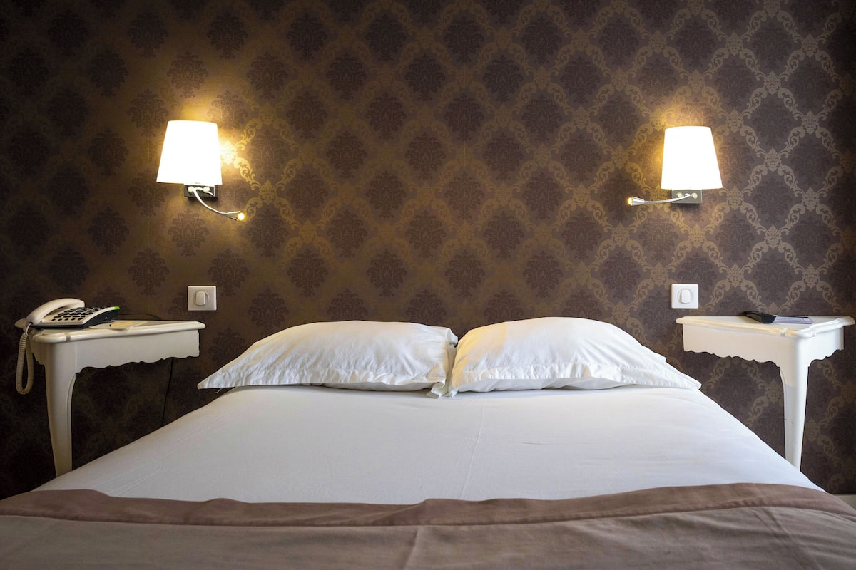 Quarto de hotel com uma cama grande, duas mesinhas de cabeceira, um telefone e duas luminárias de parede.
