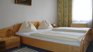 Uma cama de casal com lençóis brancos, cabeceira de madeira, mesa de cabeceira com abajur e janela com cortinas.
