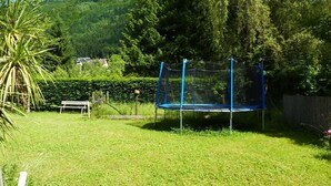 Um trampolim num gramado com um banco e uma palmeira.