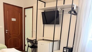 Quarto de hotel com duas camas, uma escrivaninha, uma cadeira, uma televisão e um pequeno frigorífico.