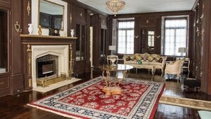 Quarto com lareira, sofá, candelabro e janelas amplas.