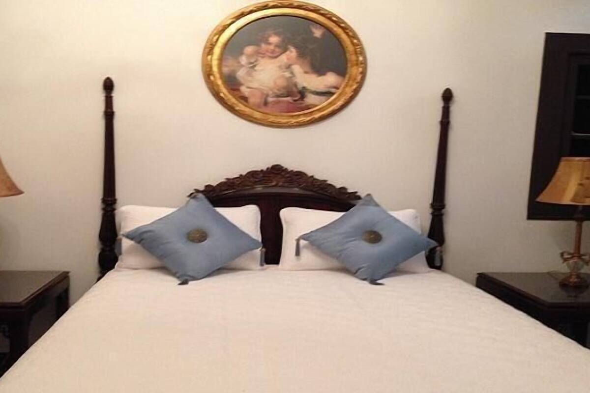 Quarto de hotel com uma cama grande, duas mesas de cabeceira, duas luminárias e um quadro na parede.