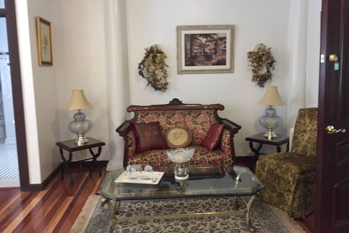 Uma sala de estar com um sofá floral, uma mesa de centro de vidro e duas luminárias.