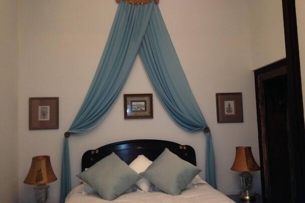 Quarto com cama, duas luminárias de cabeceira e dossel.