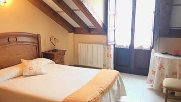 Quarto com cama, mesa de cabeceira, abajur e vista do exterior através de uma porta.