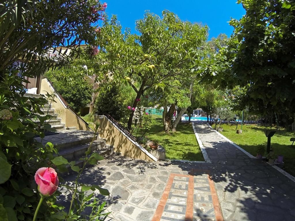 Uma trilha conduz a um edifício com escadaria de pedra e uma rosa em primeiro plano.
