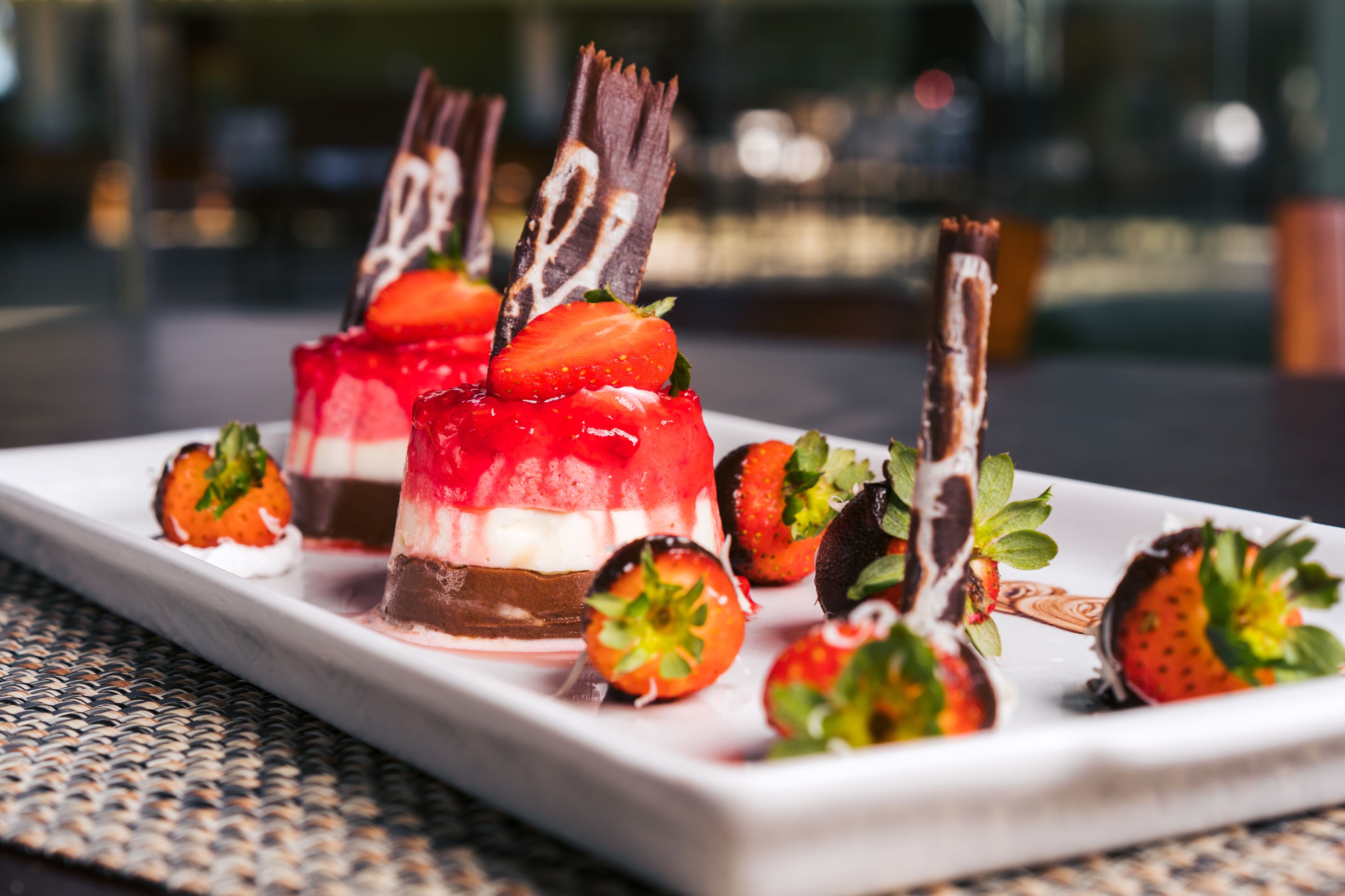 Uma bandeja de sobremesas com bolos em camadas, morangos e decorações de chocolate.