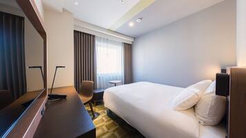 Quarto de hotel com cama, escrivaninha, cadeira, mesinha e um espelho grande.