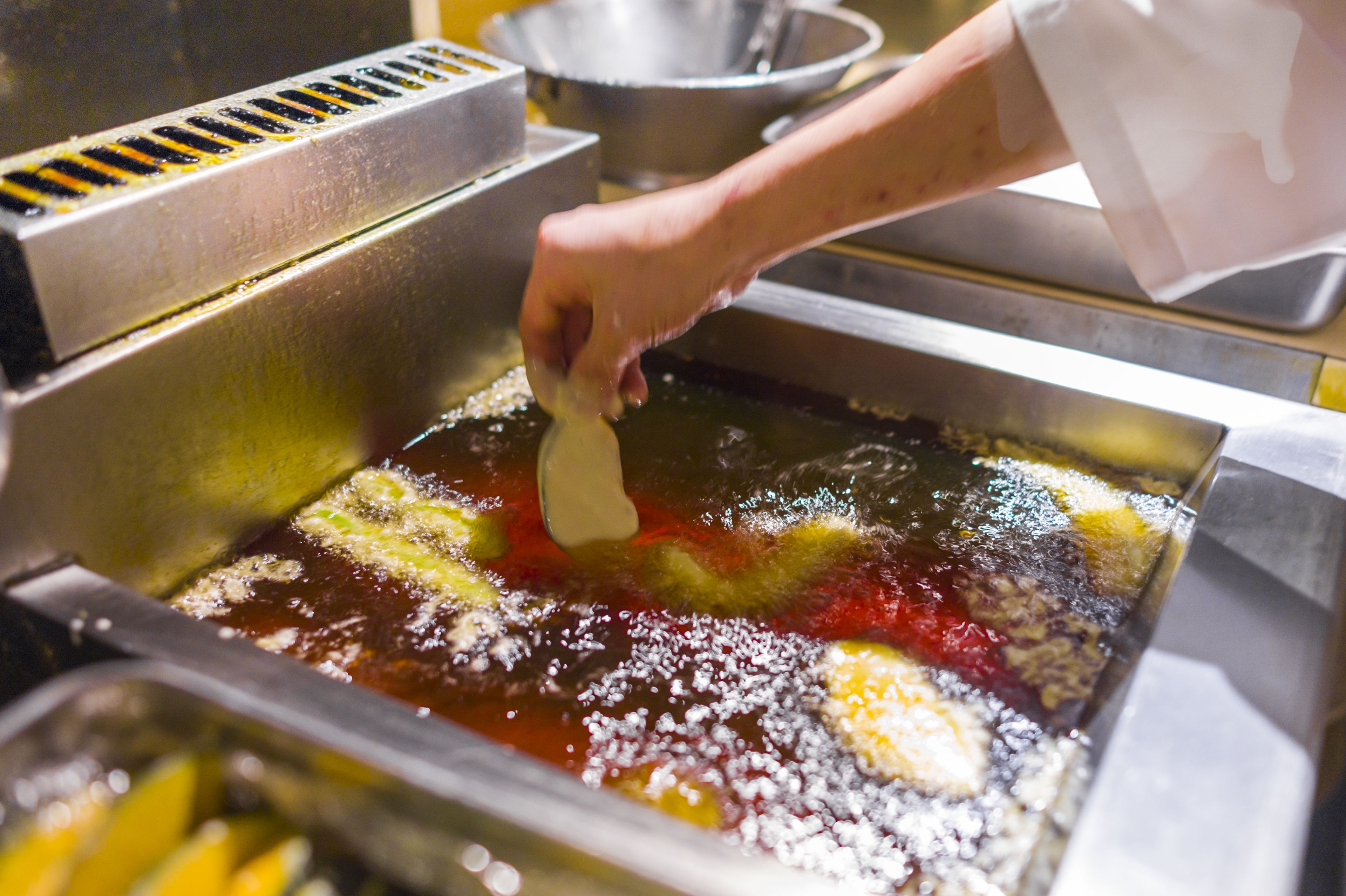 Uma mão mergulhando comida em uma fritadeira.