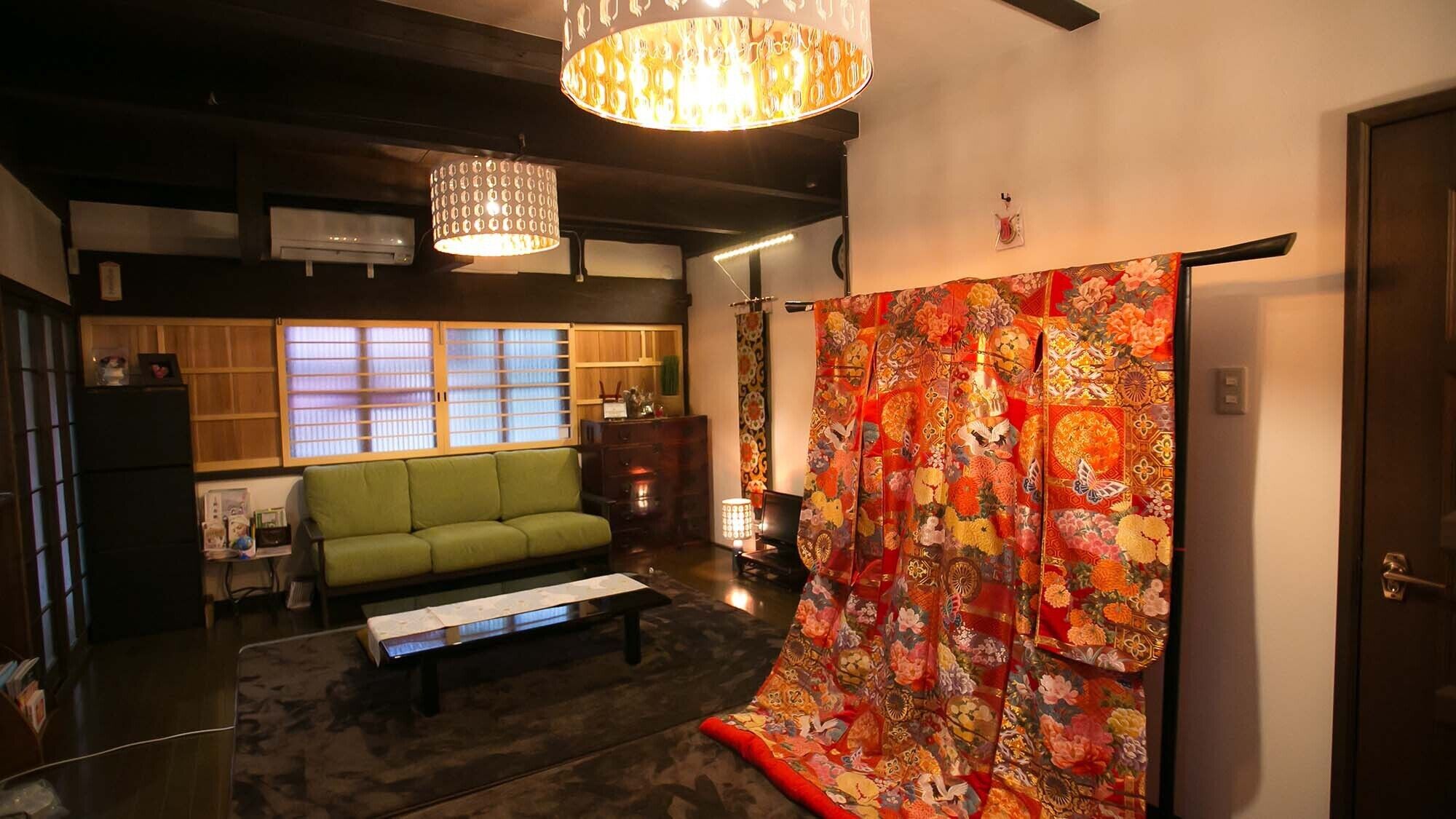 Uma sala de estar tradicionalmente japonesa com um sofá verde, uma mesa de centro de madeira e uma tapeçaria colorida.