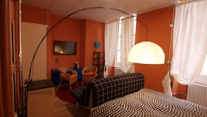Quarto com cama, escrivaninha, cadeira, televisão e janela com cortinas.