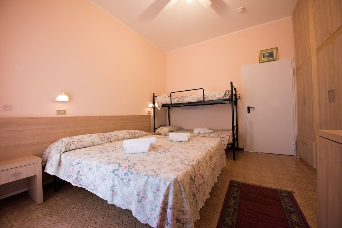 Quarto com cama beliche, mesa de cabeceira, guarda-roupa de madeira e luminária fixada na parede.