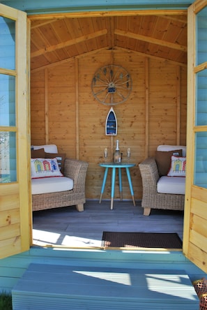 Uma cabana de madeira com dois sofás de vime, uma mesa pequena e um objeto decorativo em forma de roda na parede.