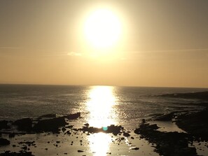 Um pôr do sol sobre uma praia com pedras em primeiro plano.
