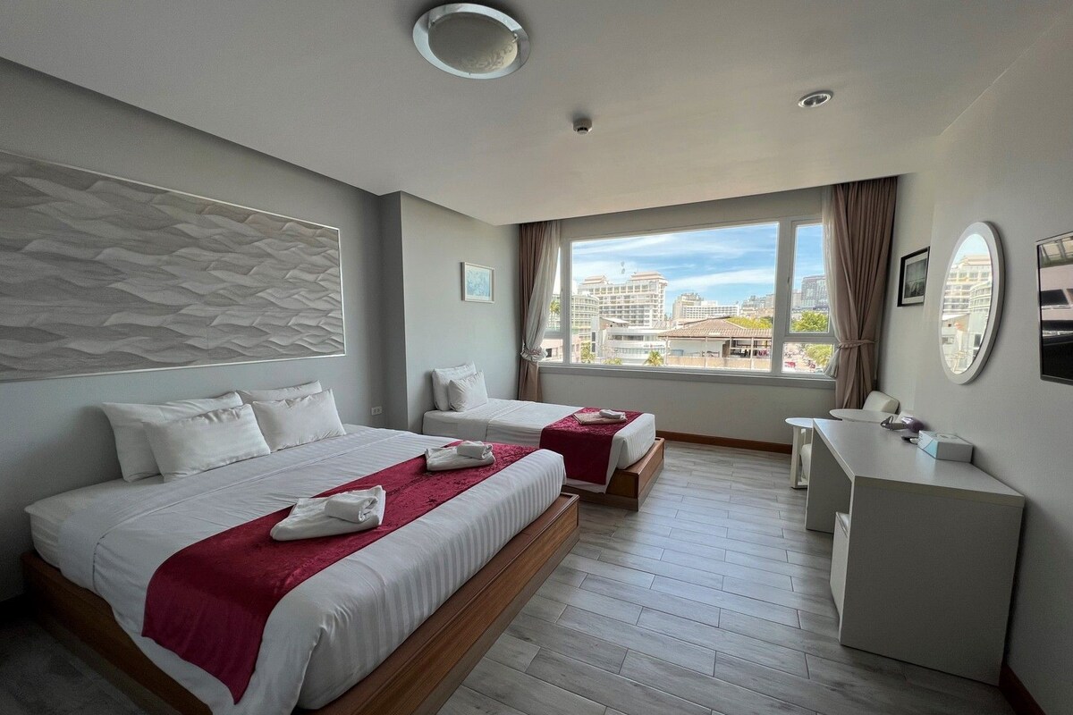 Quarto de hotel com duas camas, uma escrivaninha e uma janela grande com vista para a cidade.