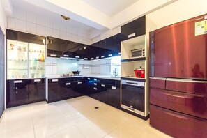Cozinha moderna com armários pretos, bancadas brancas e eletrodomésticos em aço inoxidável, incluindo geladeira e forno.