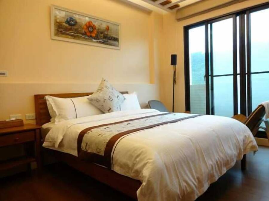 Quarto com cama, mesa de cabeceira, cadeira e janela com vista.