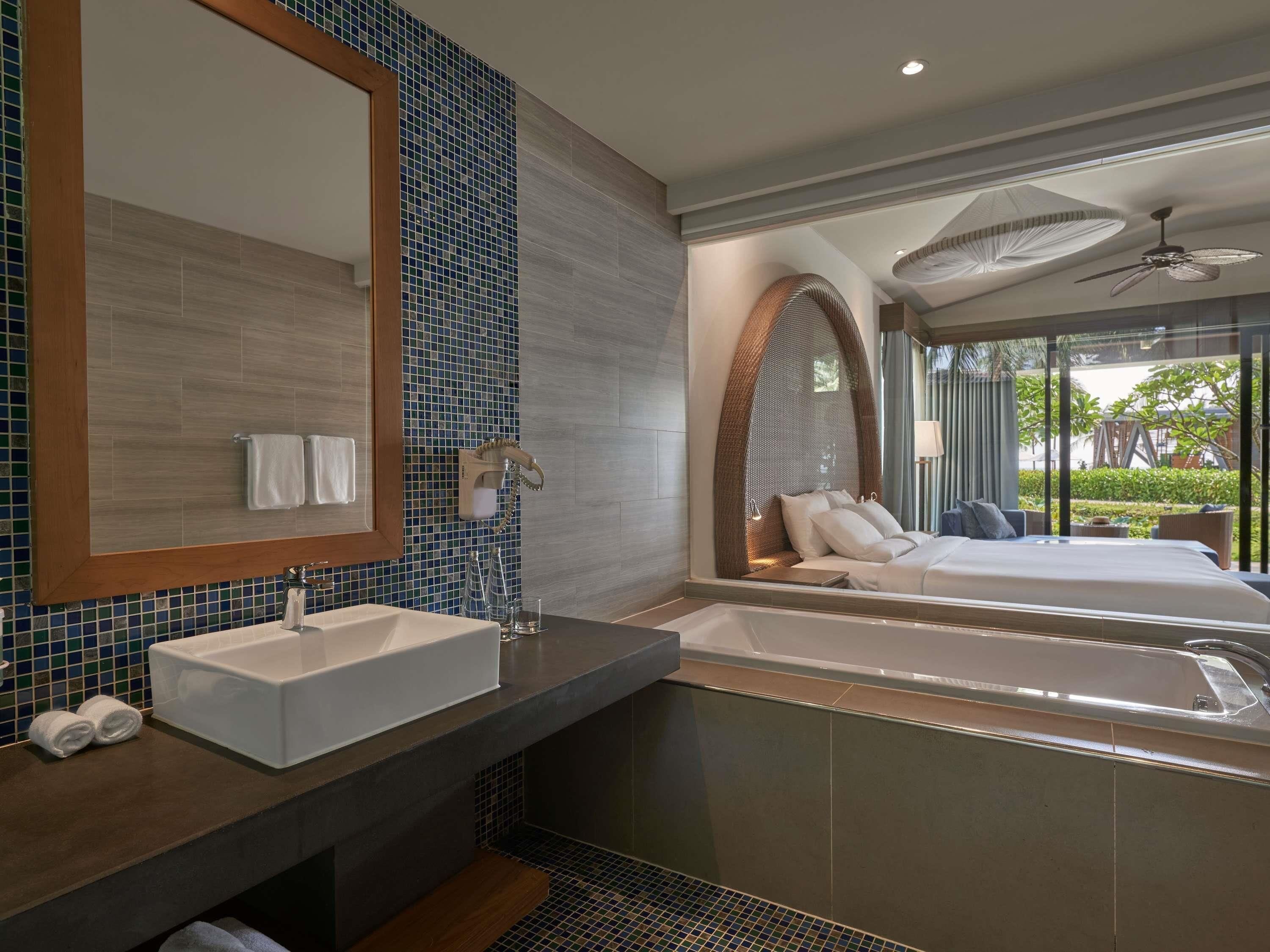 Uma casa de banho moderna com um espelho grande, duas sanitas, uma banheira e uma cama com vista para o exterior.