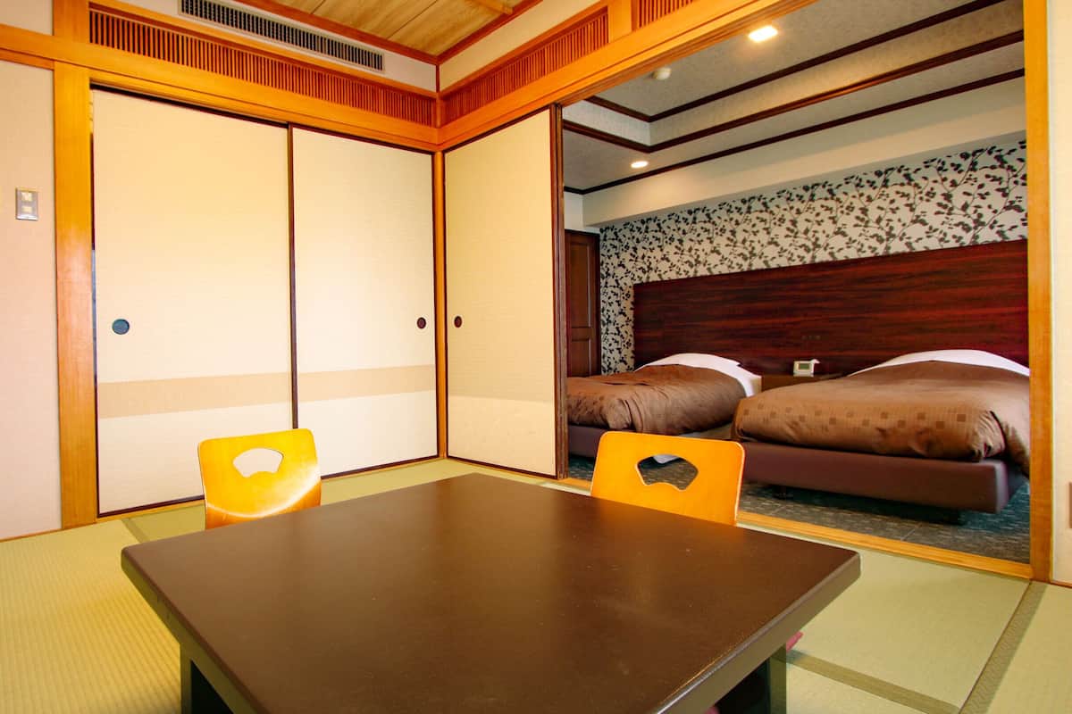 Um quarto japonês tradicional com tatames, uma mesa baixa e uma cama com cabeceira de madeira.