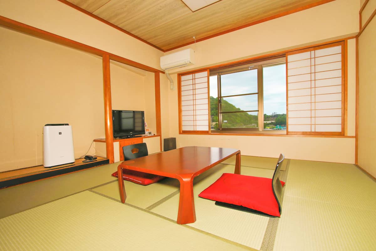 Um quarto japonês tradicional com tatames, uma mesa baixa, uma televisão e um frigorífico.
