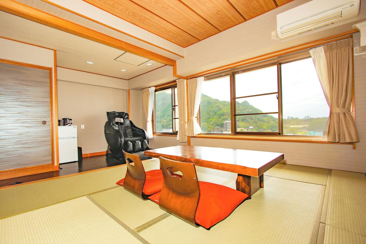 Um quarto japonês tradicional com tatames, uma mesa baixa e uma cadeira preta com almofadas laranja.