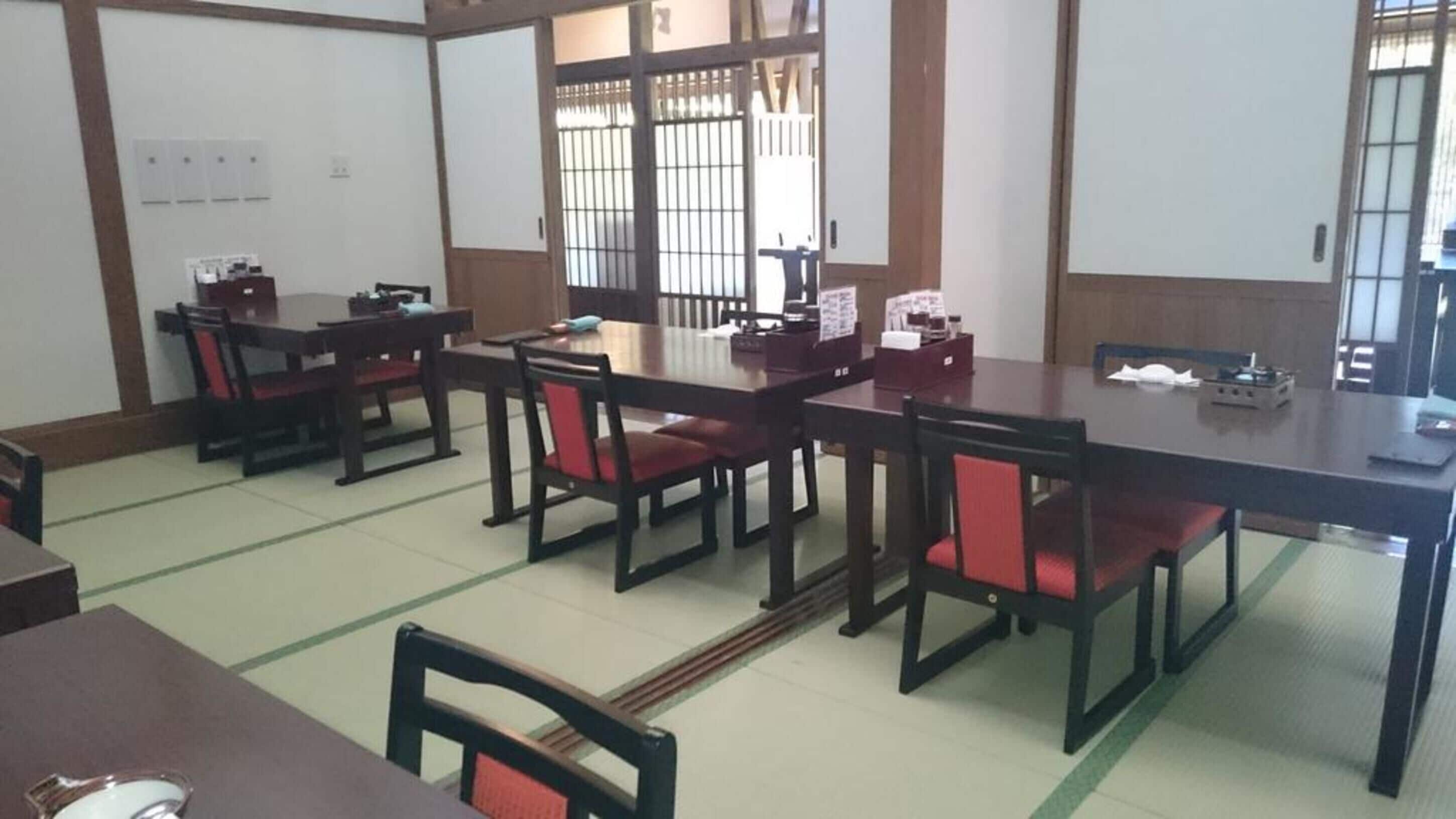 Quarto em estilo japonês tradicional, com tatames, mesinhas baixas e cadeiras acolchoadas vermelhas.