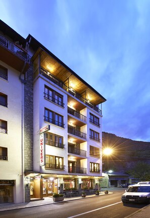 Um hotel com vários andares, varandas, uma placa indicando que é um hotel e uma entrada bem iluminada.