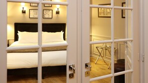 Quarto de hotel com cama, piso de madeira e porta com moldura branca.