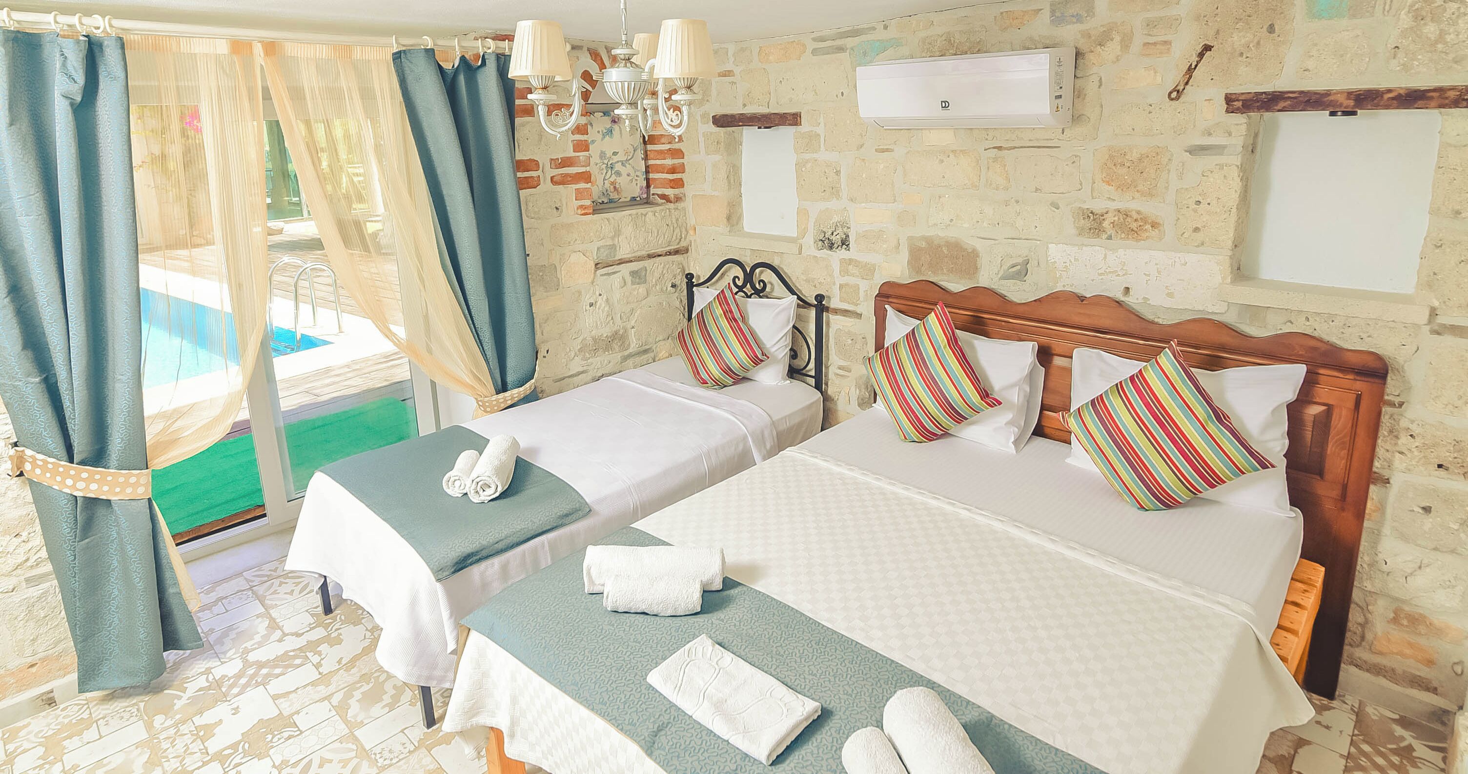 Quarto de hotel com duas camas, parede de pedra, piscina e ventoinha no teto.