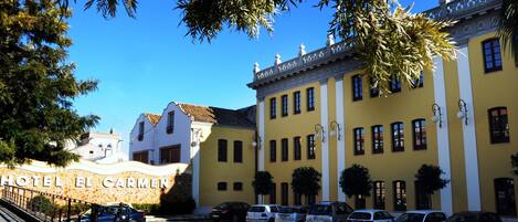 Hotel com fachada amarela, carros estacionados e céu azul.