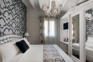 Quarto de hotel com uma cama grande, um candelabro, uma televisão e papel de parede estampado.