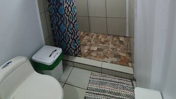 Um banheiro pequeno com vaso sanitário, chuveiro com cortina estampada e piso revestido.
