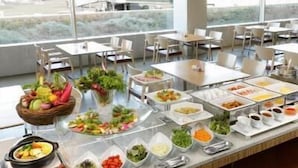 Espaço de buffet com diversas opções de comida e vista para o aeroporto ao fundo.