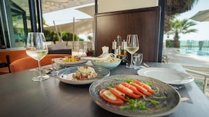 Mesa de jantar com diversos pratos, copos de vinho e vista para uma piscina externa.