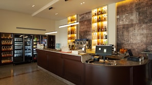 Uma área de bar com balcão, geladeiras cheias de bebidas e uma parede com prateleiras de garrafas.