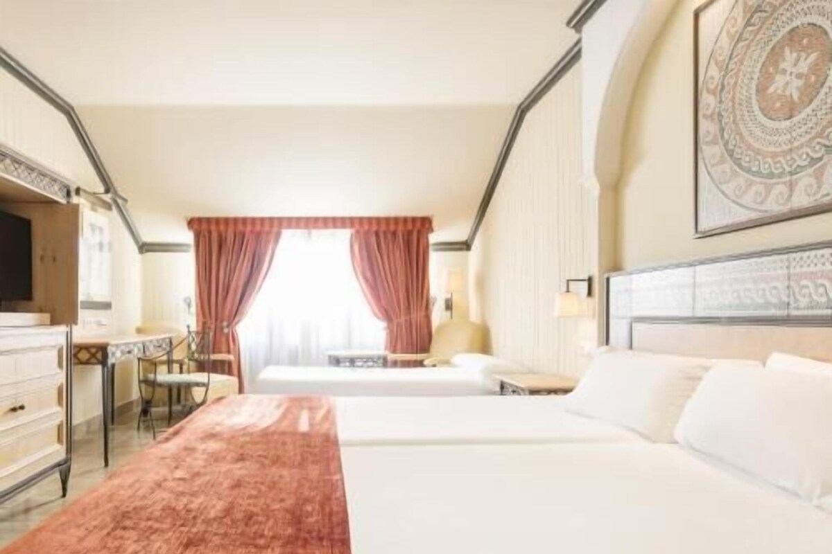 Quarto de hotel com uma cama grande, uma escrivaninha com cadeira, televisão e janela com cortinas.