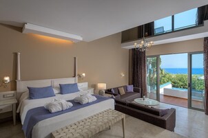Quarto de hotel moderno com uma cama grande, um sofá, uma mesinha e uma varanda com vista para o mar.