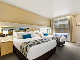 Quarto de hotel com uma cama grande, duas mesas de cabeceira, um sofá, uma televisão e uma janela com cortinas.