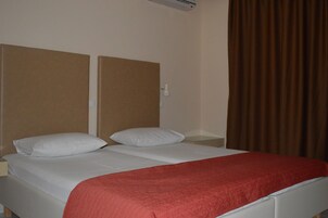 Uma cama com um cobertor vermelho, almofadas brancas e uma cabeceira.