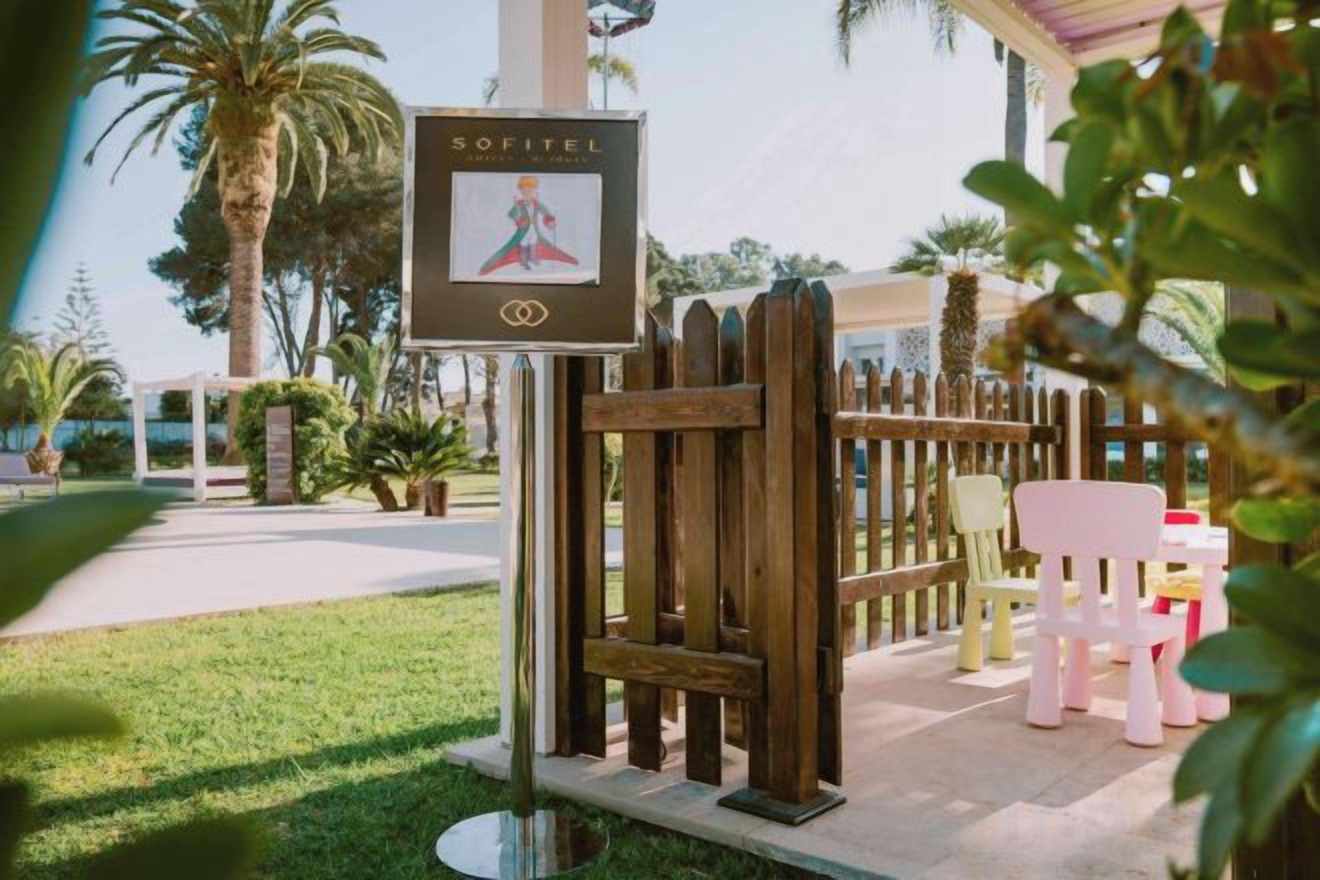 Um portão de madeira com uma placa indicando 'SOFITEL' e uma palmeira ao fundo.