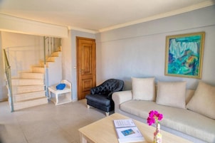 Uma sala de estar com escada, uma poltrona de couro preto, um sofá bege e um quadro na parede.