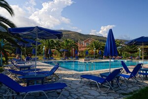 Uma área à beira da piscina com espreguiçadeiras azuis e guarda-sóis, céu limpo e uma montanha ao fundo.