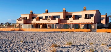 Um hotel à beira-mar com várias varandas, grandes janelas e uma praia arenosa em primeiro plano.