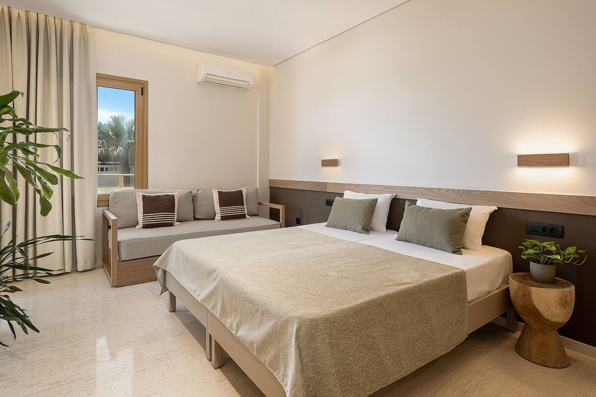 Quarto de hotel moderno com uma cama grande, um sofá e uma planta em vaso.