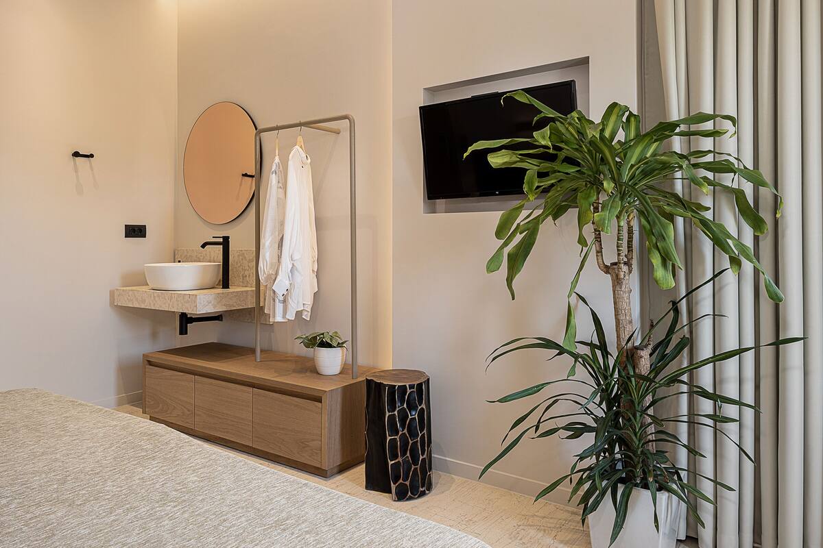 Quarto moderno com cama, mesa de cabeceira, espelho, televisão e planta em vaso.