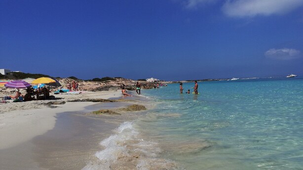 Uma praia com águas turquesa cristalinas, pessoas nadando e guarda-sóis.