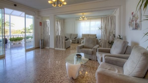 Uma sala de estar ampla com teto alto, um candelabro e vista para área externa através de grandes portas de vidro.