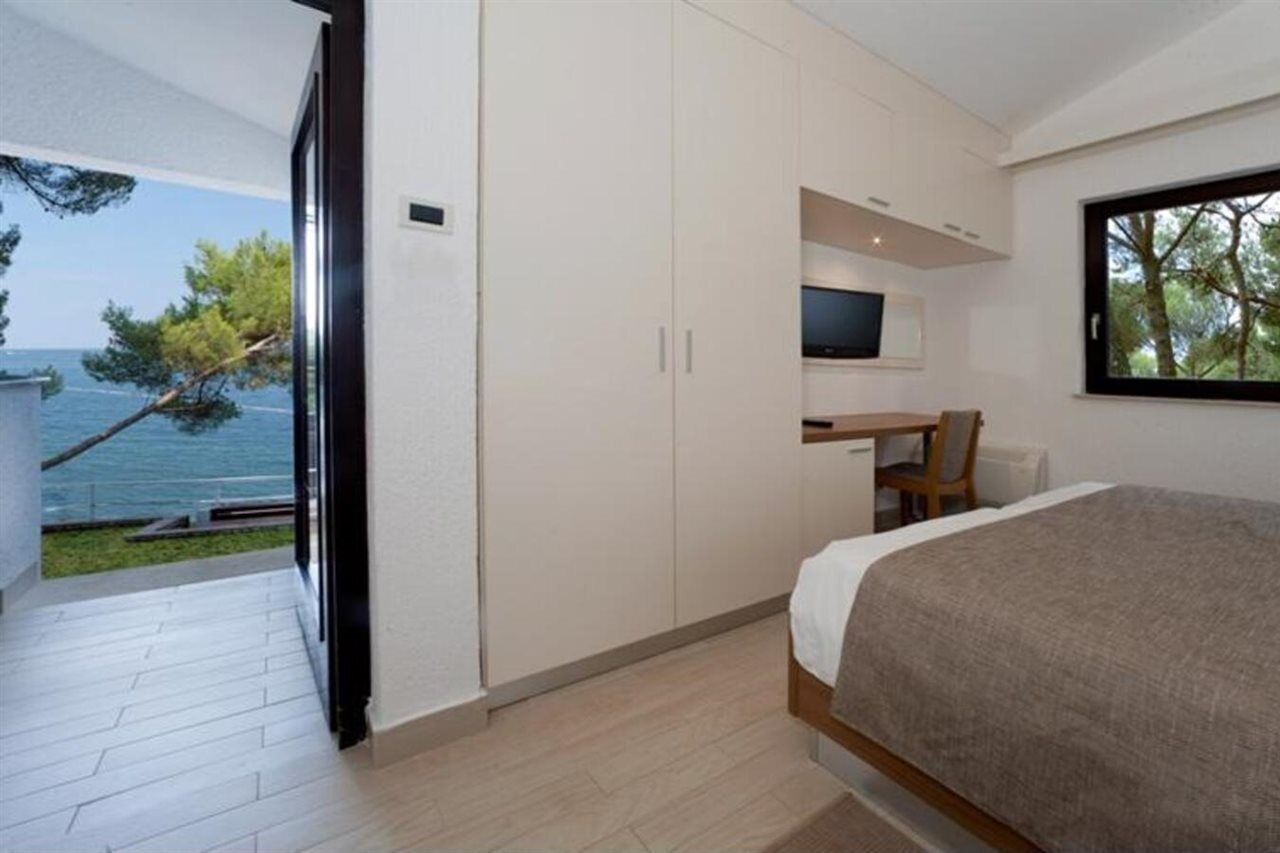 Quarto com cama, escrivaninha e televisão. Tem vista para o mar e para árvores.