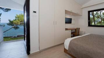 Quarto com cama, escrivaninha e televisão. Tem vista para o mar e para árvores.
